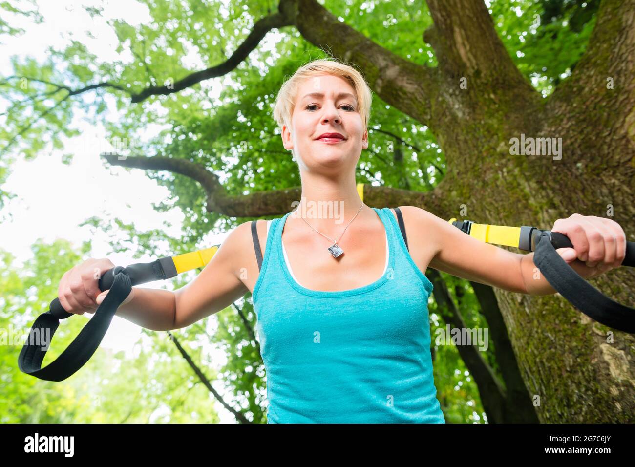 Young woman exercising with suspension trainer sling in City Park under ...