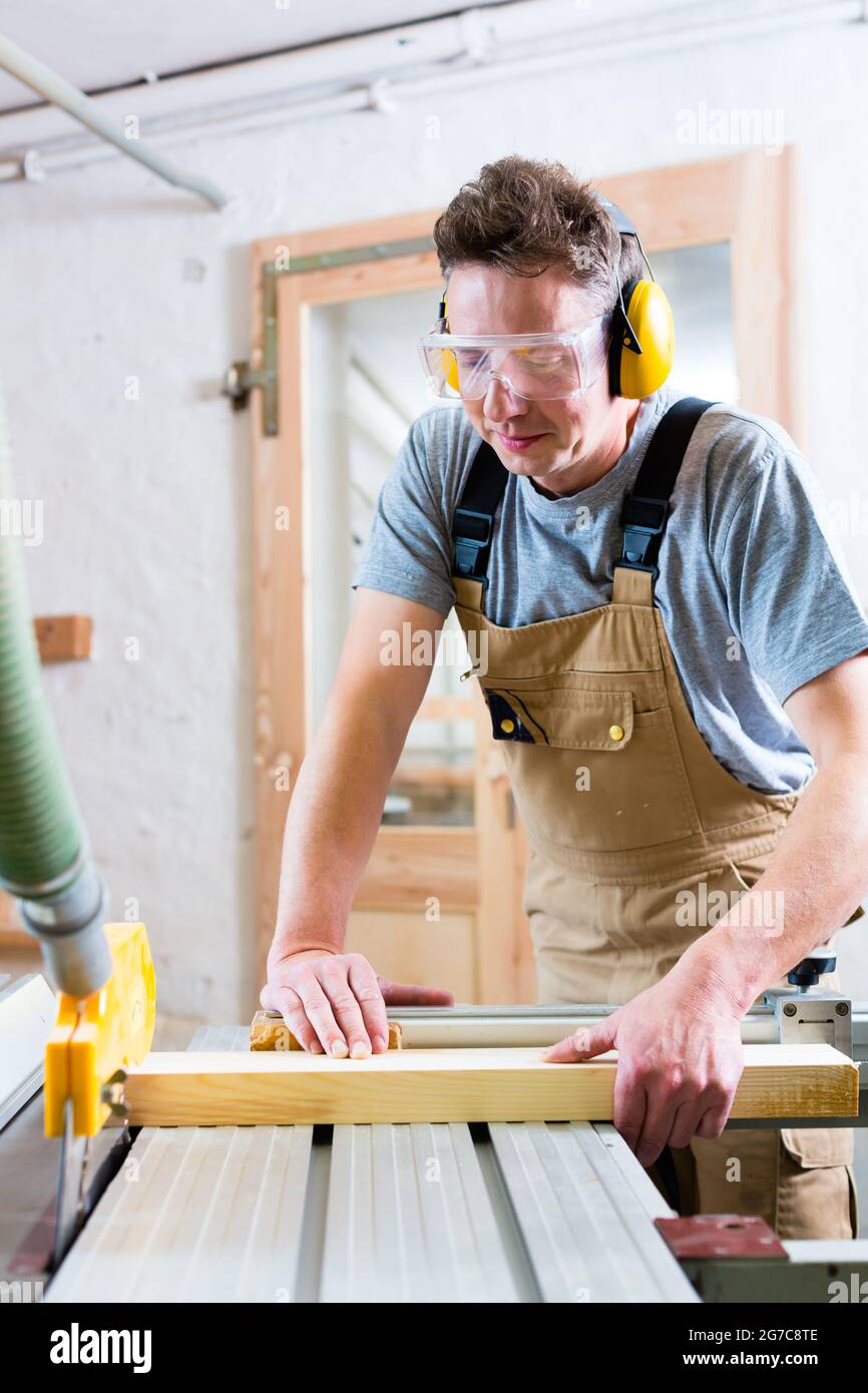 Carpenter working on an electric buzz saw cutting some boards, he is ...