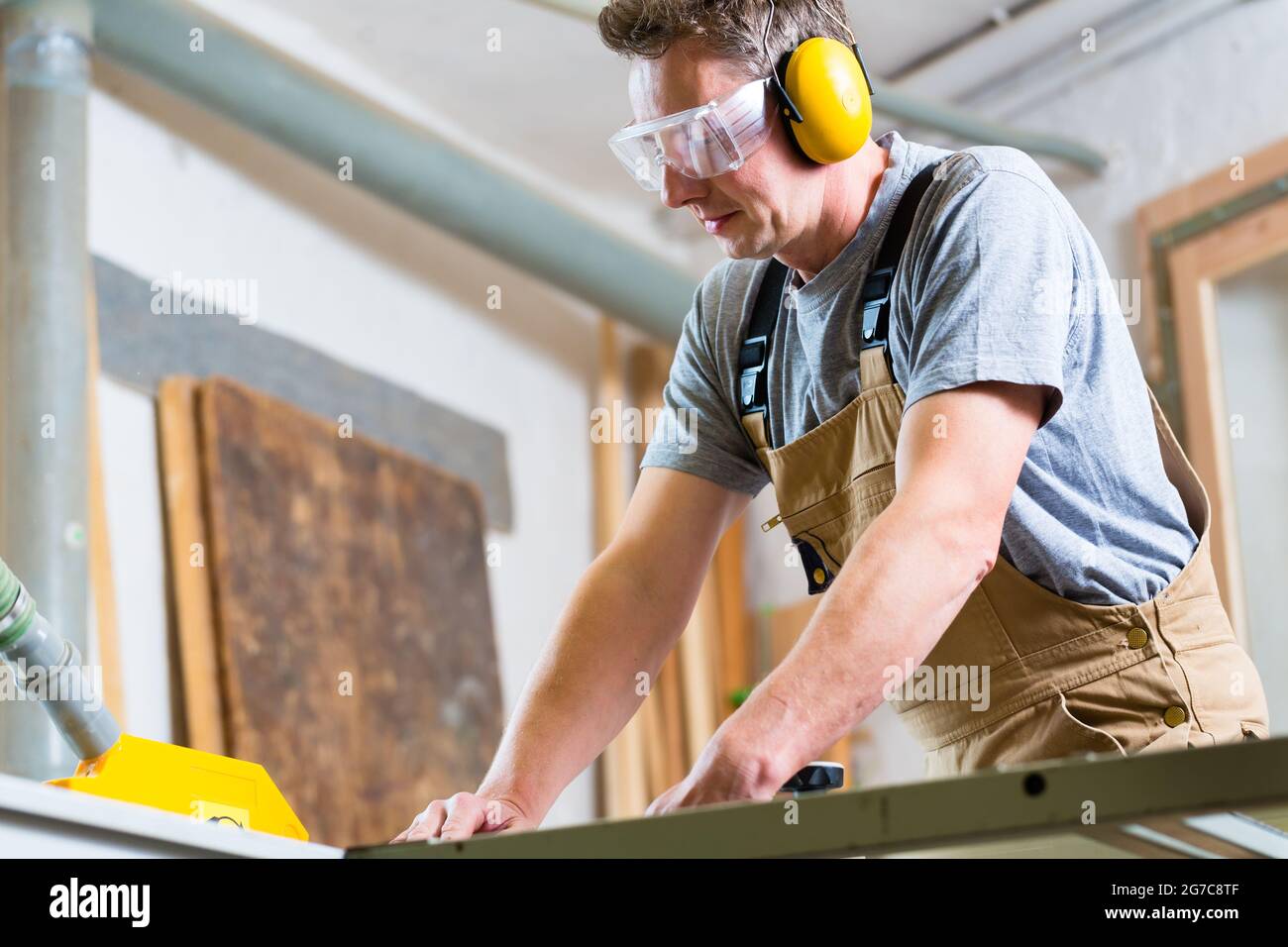 Carpenter working on an electric buzz saw cutting some boards, he is ...