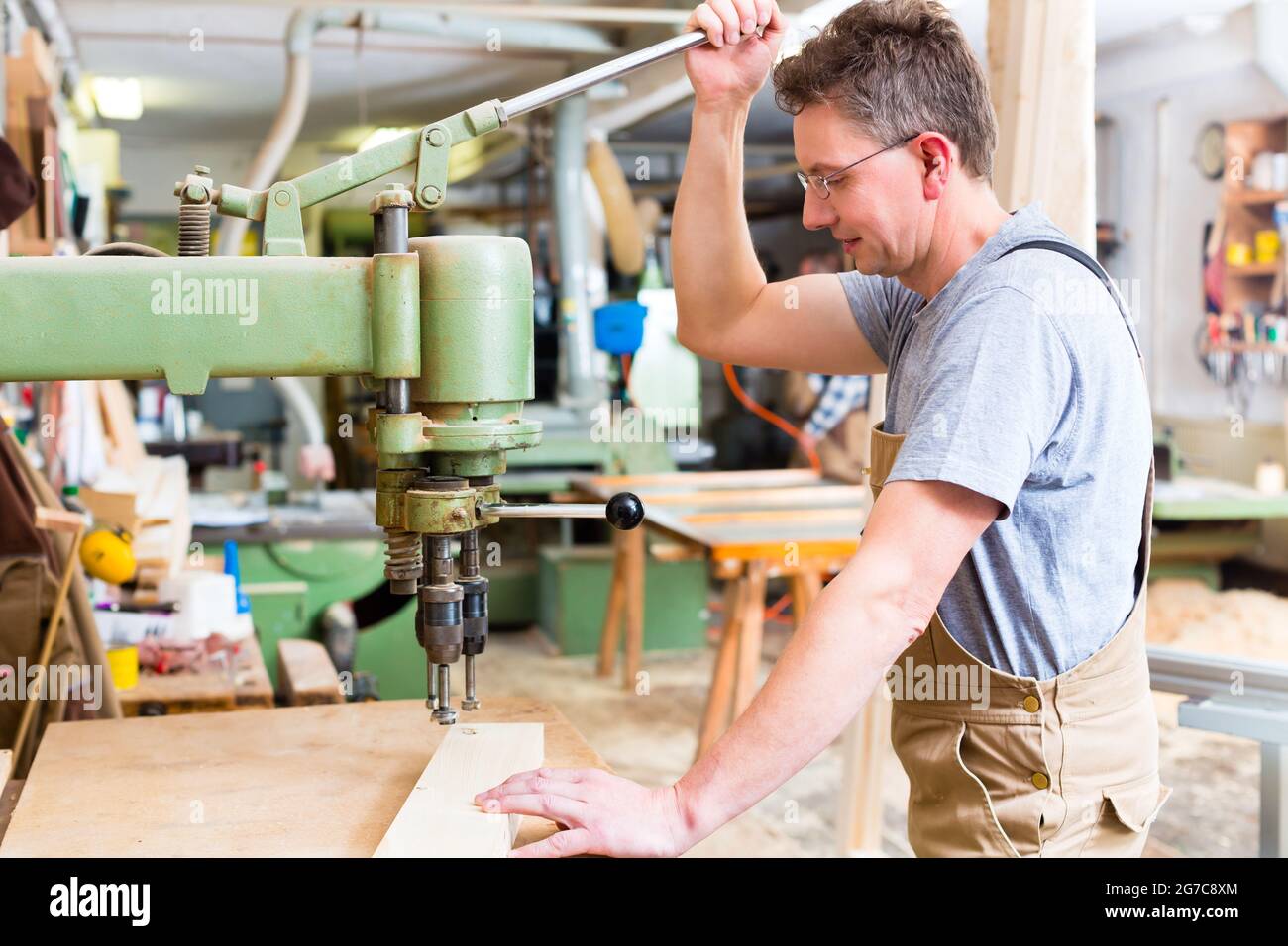 Carpenter working on an electric bench drill, drilling some boards ...