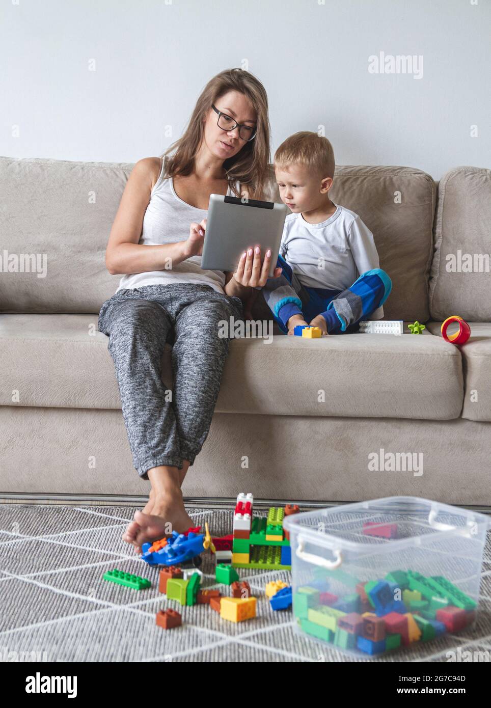 mom and child with tablet spend time together sitting on sofa at home ...