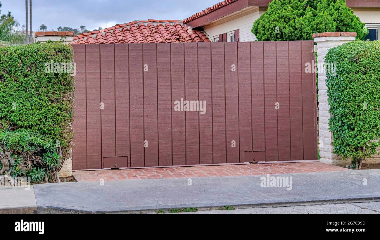 Pano Brown gate and white brick fence against red tile roof of house in ...