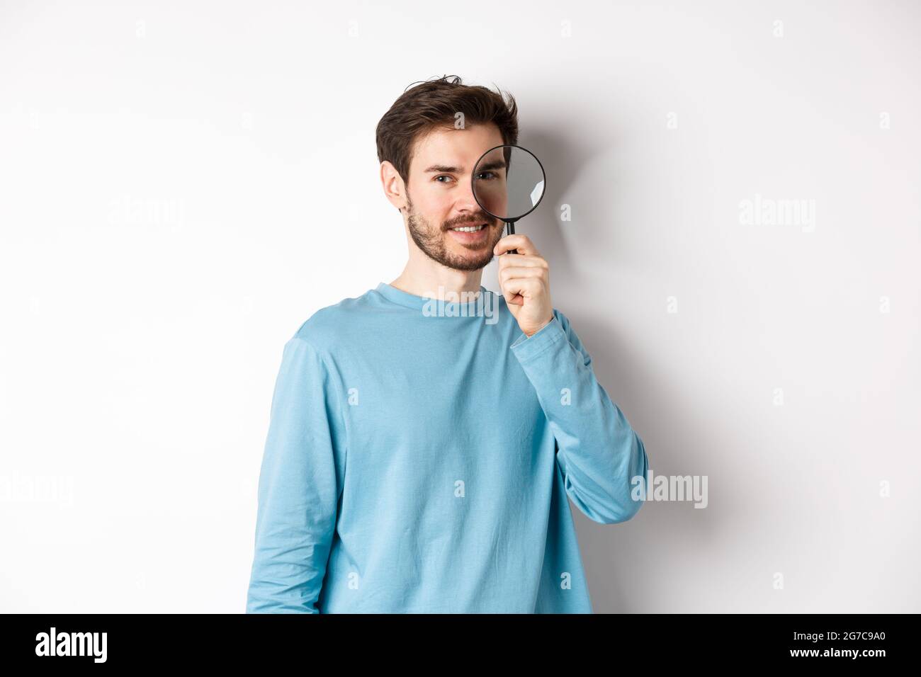 Smiling young man detective looking through magnifying glass, searching ...