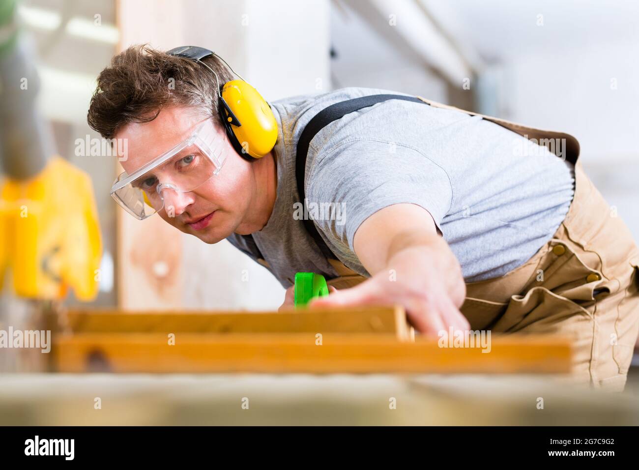 Carpenter working on an electric buzz saw cutting some boards, he is ...