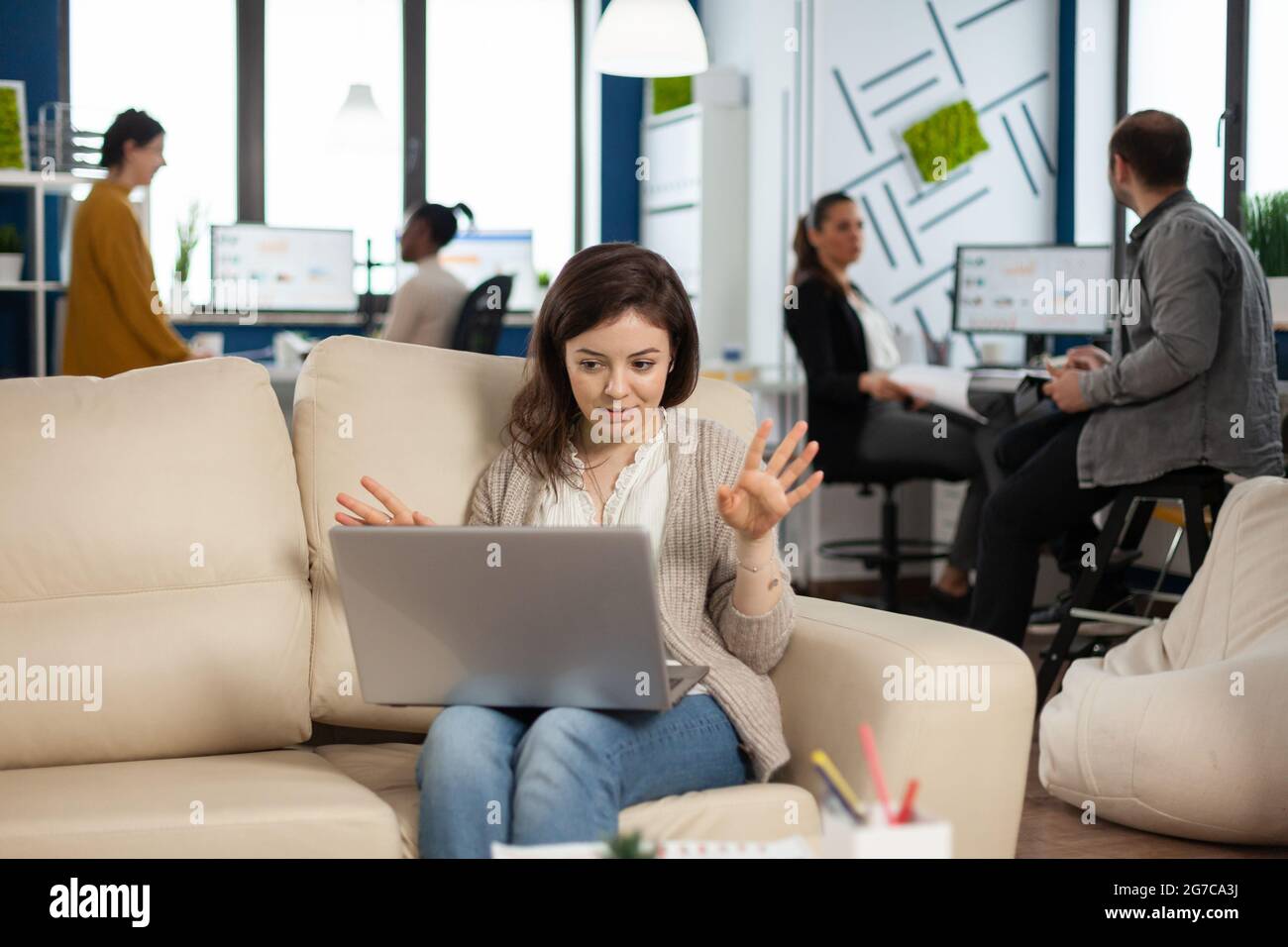 Manager woman sitting on couch holding laptop and talking on video call ...