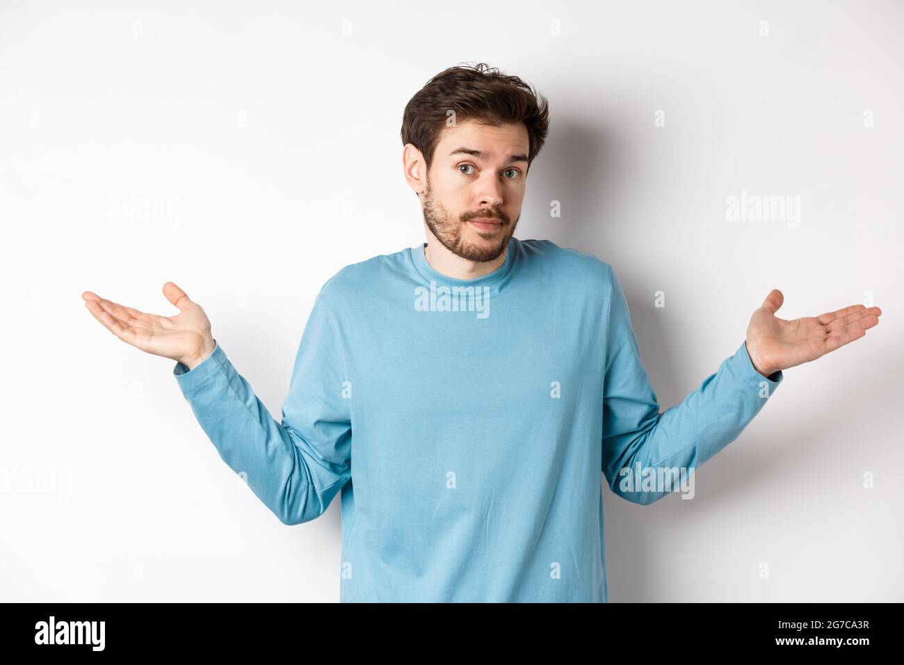 Clueless bearded guy in blue shirt, shrugging shoulders and looking ...