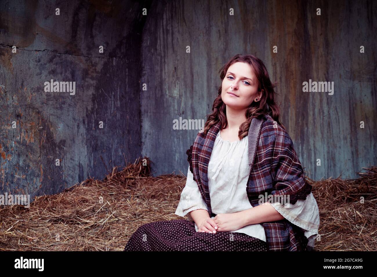 Young woman in retro clothes sits on an old hayloft, portrait of a ...