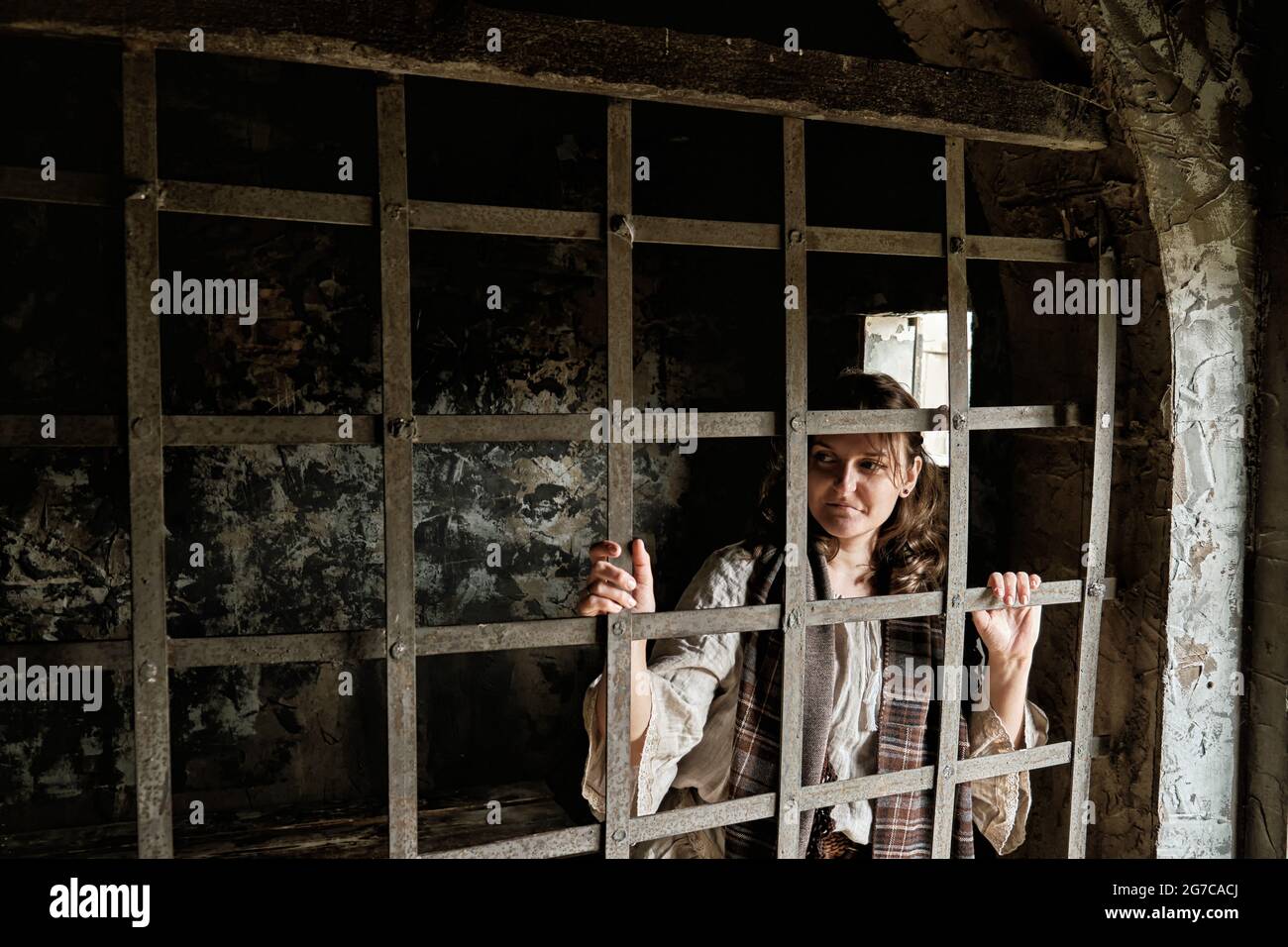 A young woman stands behind the bars of an ancient prison cell ...