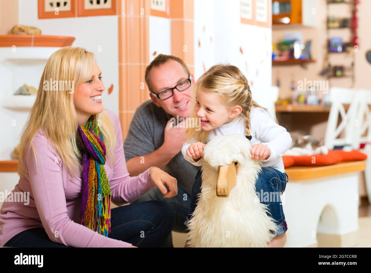 Parents and daughter rocking and playing with rocker horse in living ...