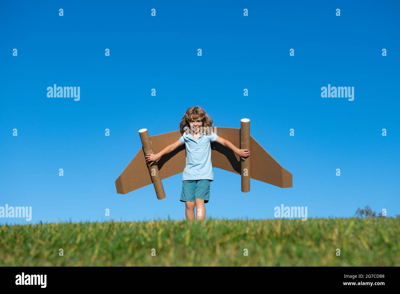 Happy child playing outside on green grass and blue sky. Kid pilot with ...
