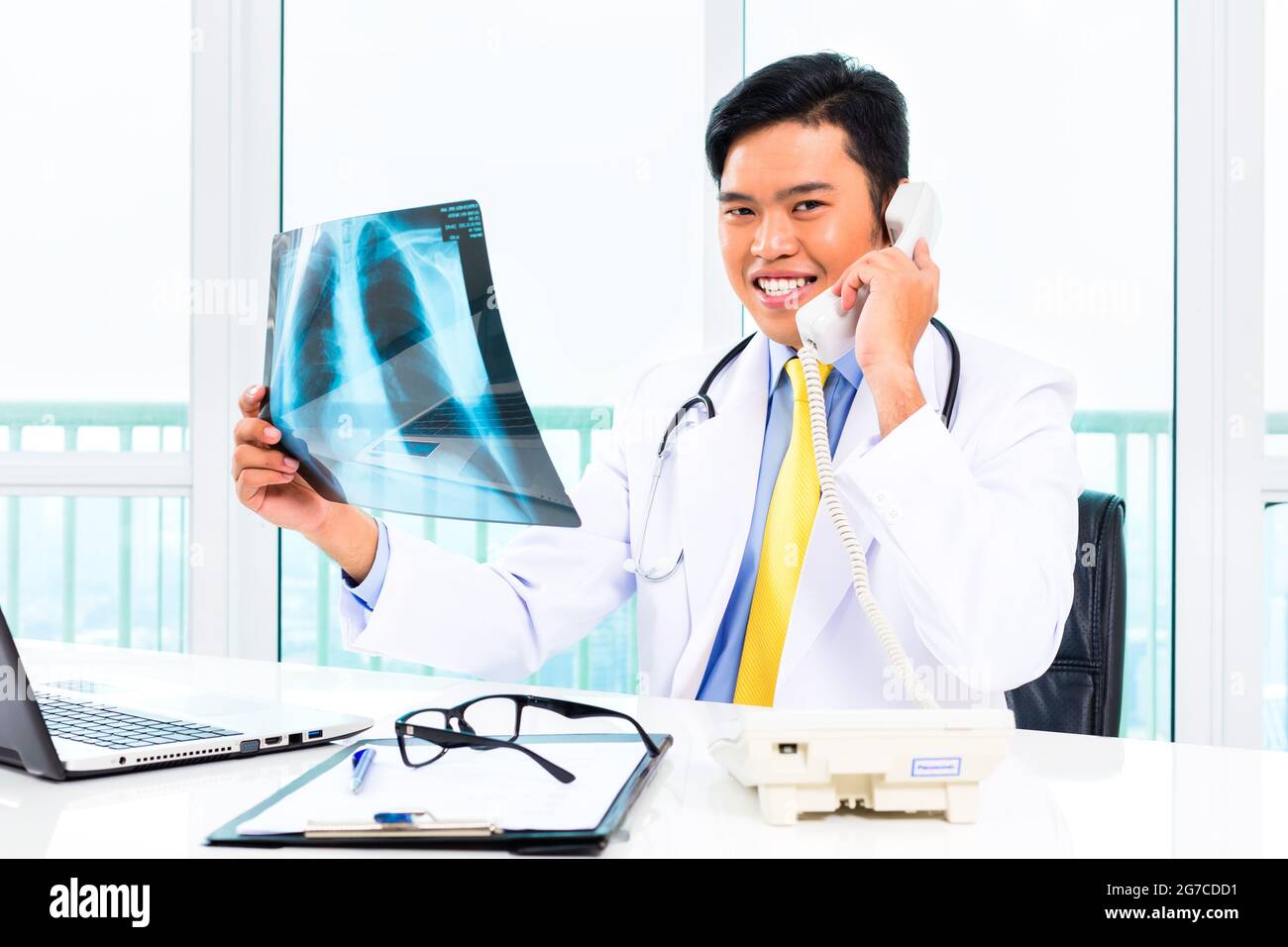 Asian doctor telephoning about diagnosis X-ray photograph in his ...