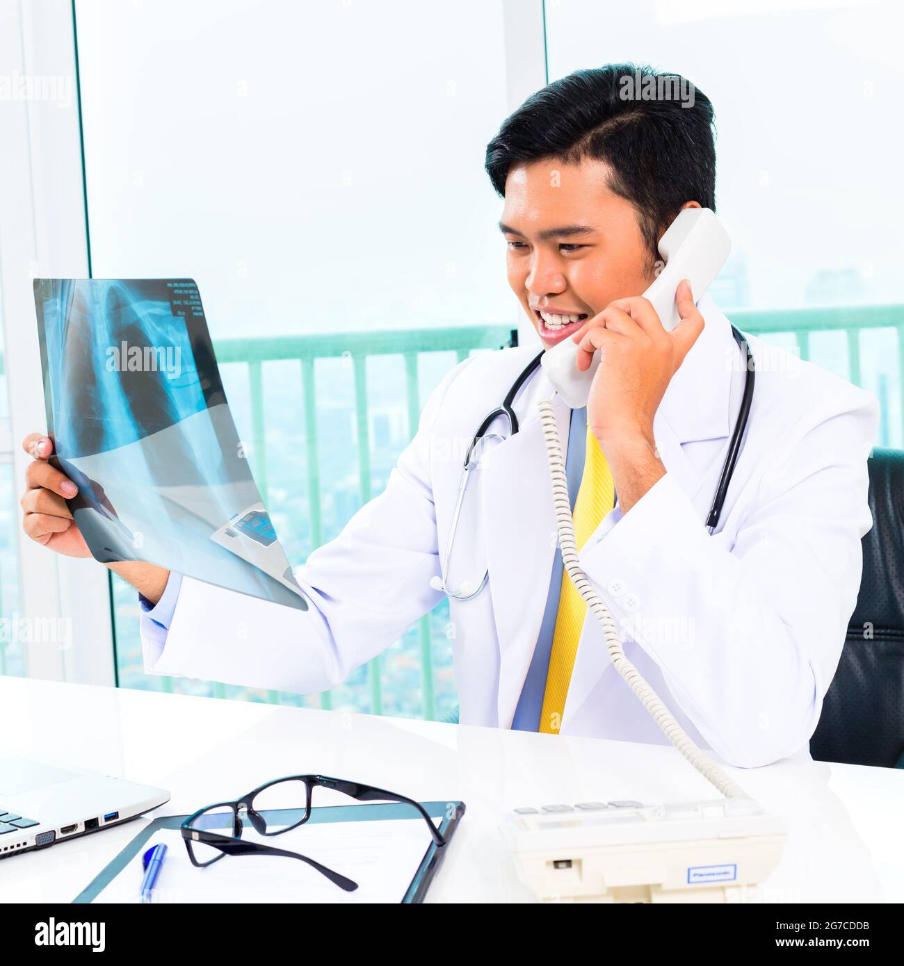 Asian doctor telephoning about diagnosis X-ray photograph in his ...