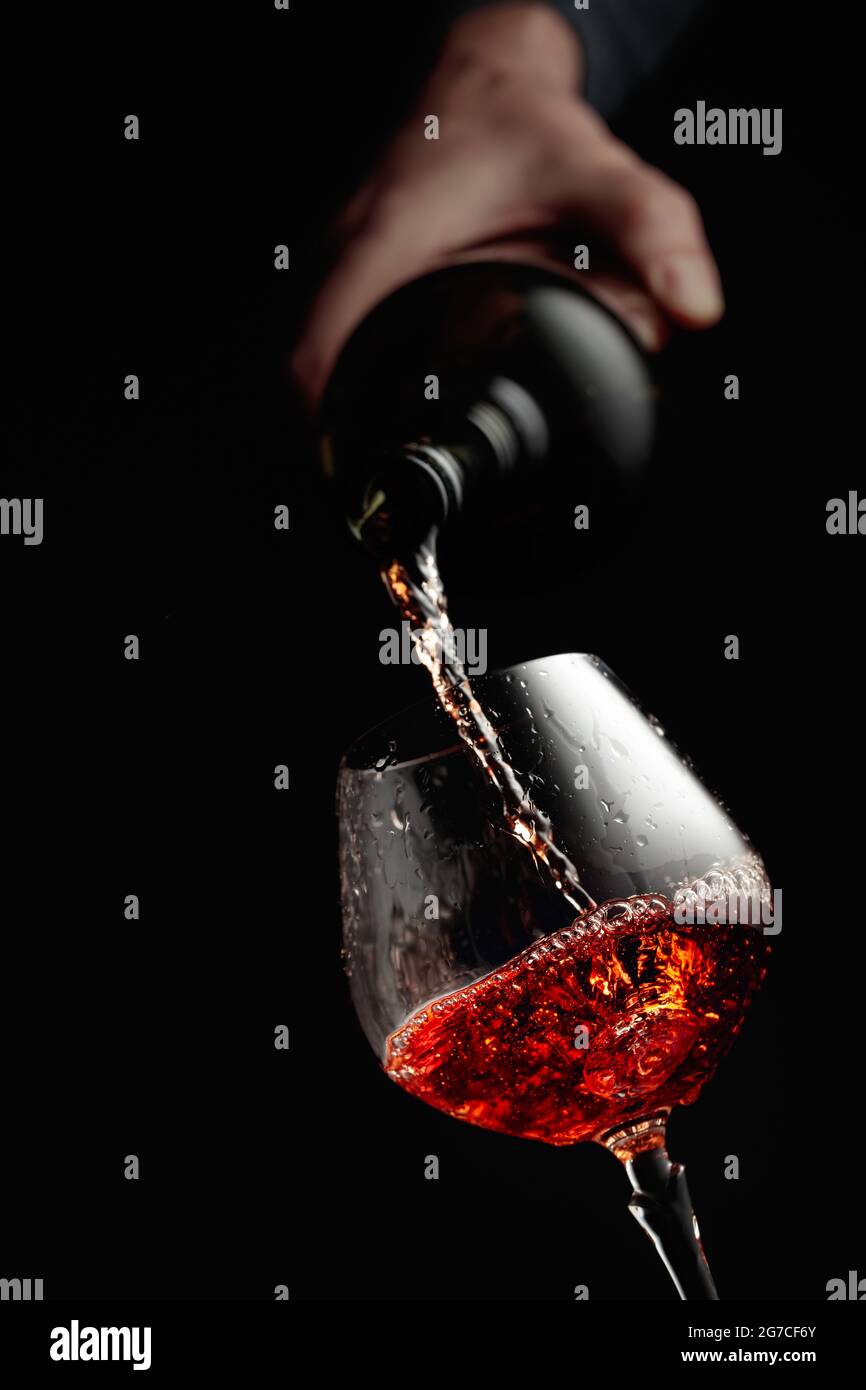 Pouring brandy in a glass goblet. Black background with copy space ...