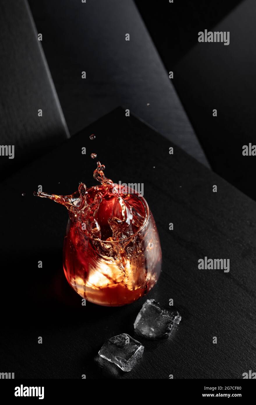 Ice cubes fall into a glass of whiskey creating splashes Stock Photo - Alamy