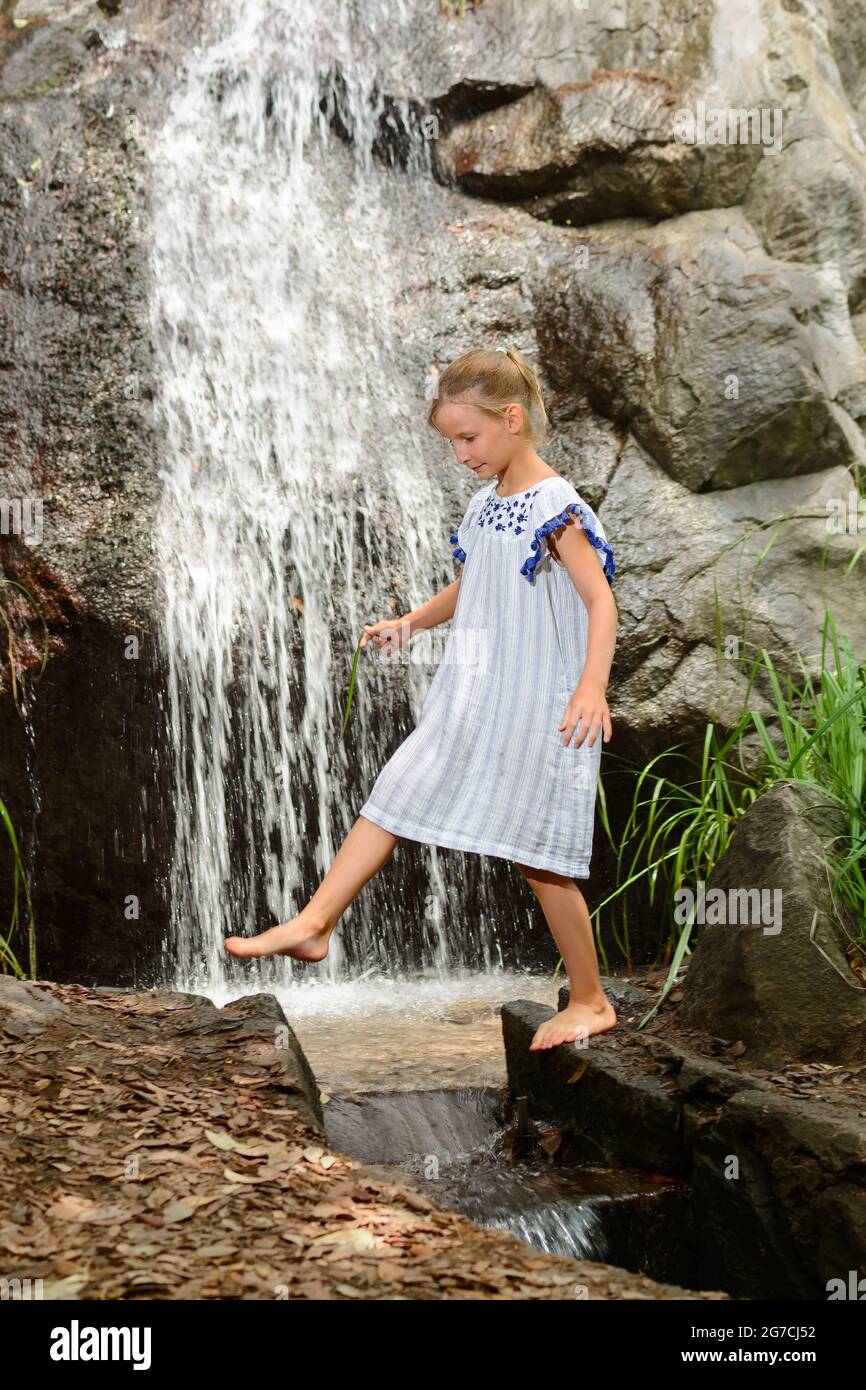 Teen girl jumping over stream from rock to rock to overpass the ...
