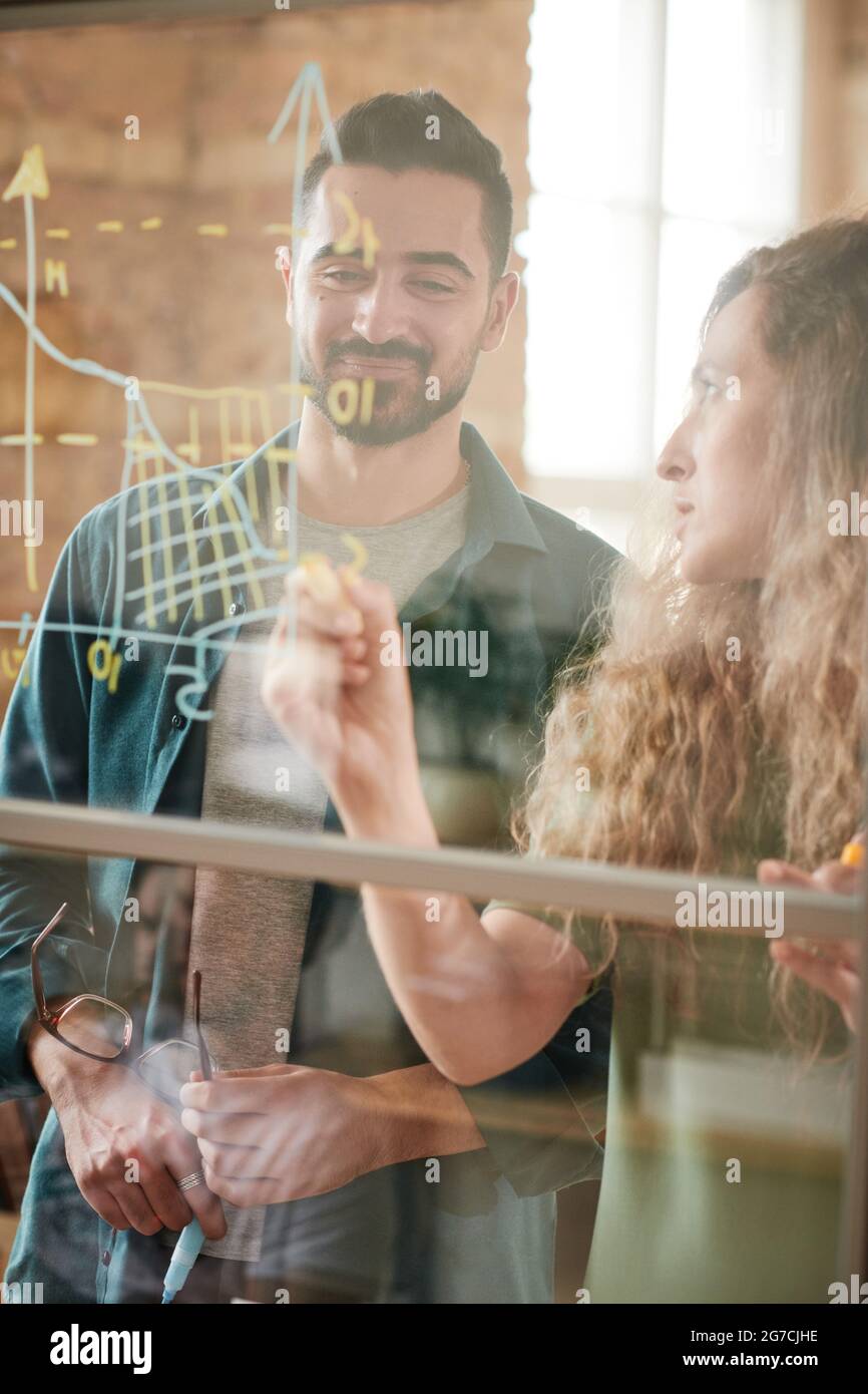 Business partners drawing graphic on glass wall and discussing it ...