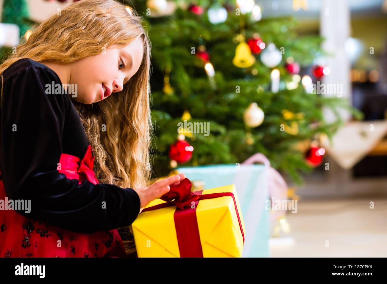 Girl opening present on Christmas day under tree Stock Photo - Alamy