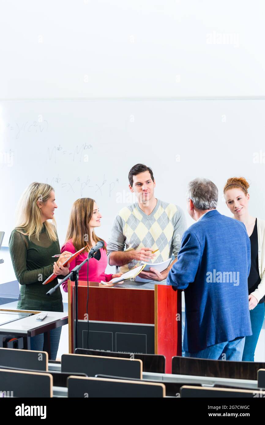 College students making lesson notes while asking professor in ...