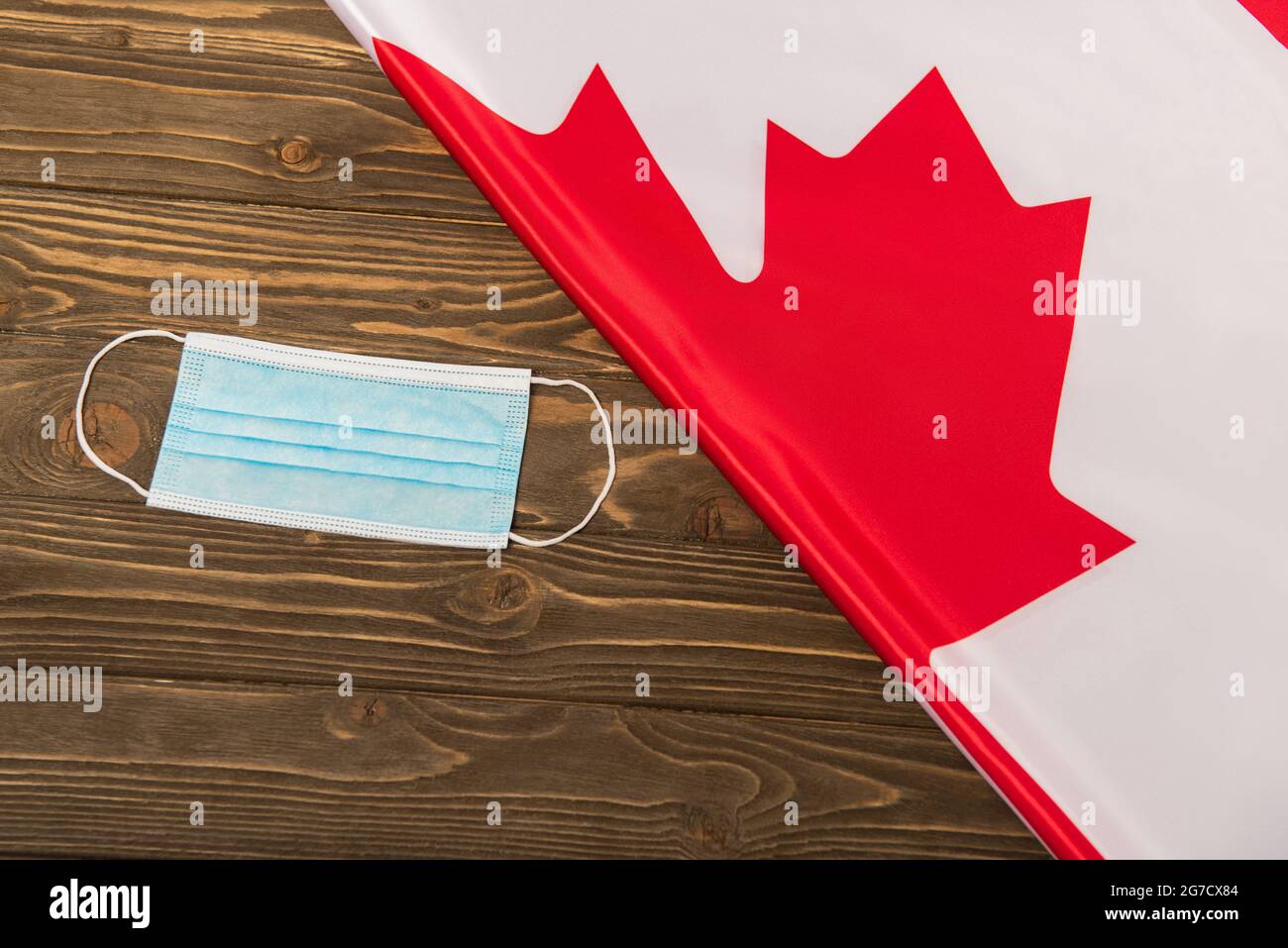 top view of canadian flag and medical mask on wooden surface, covid-19 ...