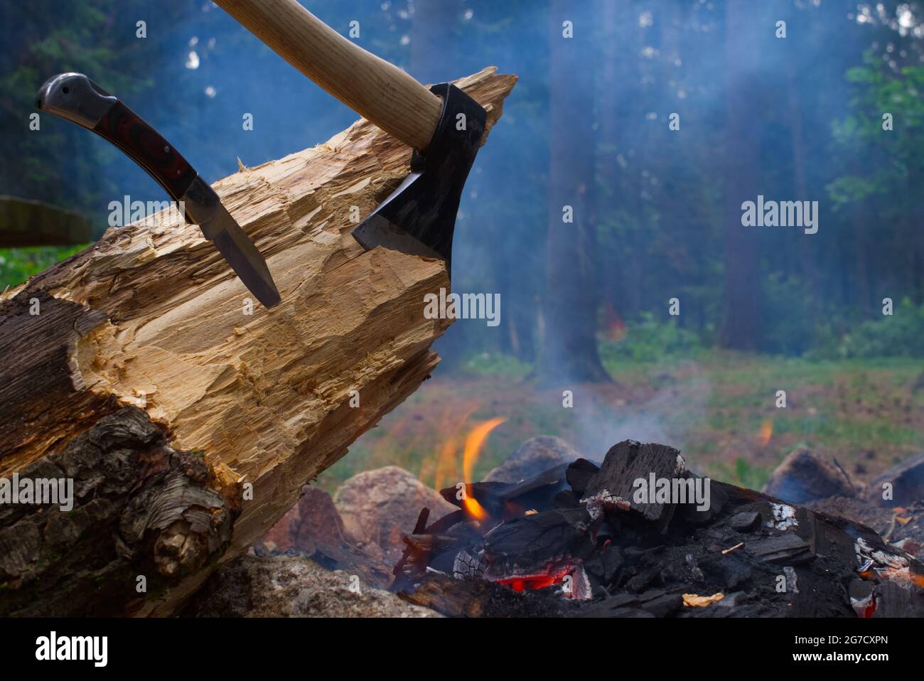 Camp fire in a forest with chopper and folding pocket knife lodged in a ...