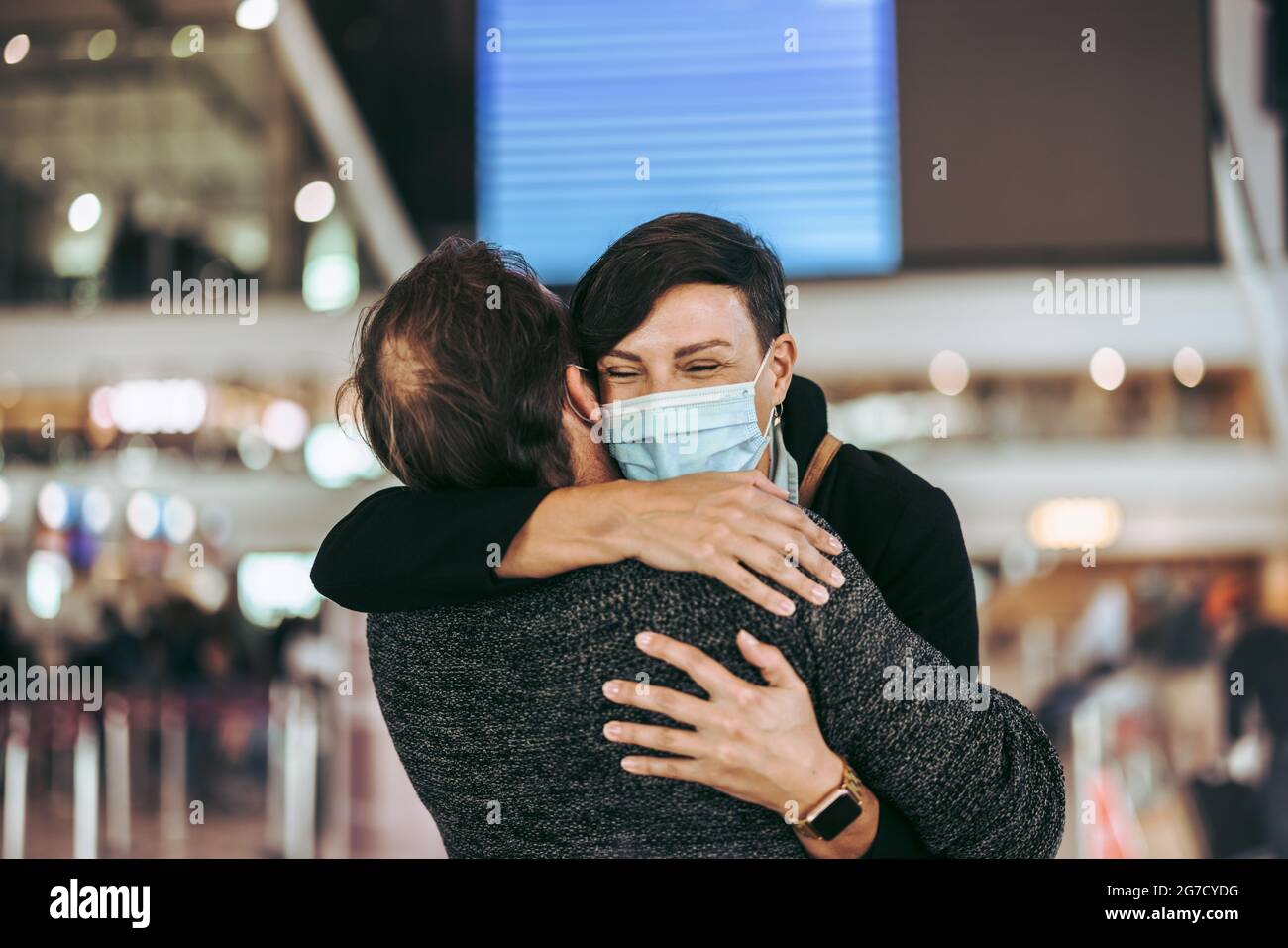 Husband and wife embracing at airport during pandemic. Woman in face ...