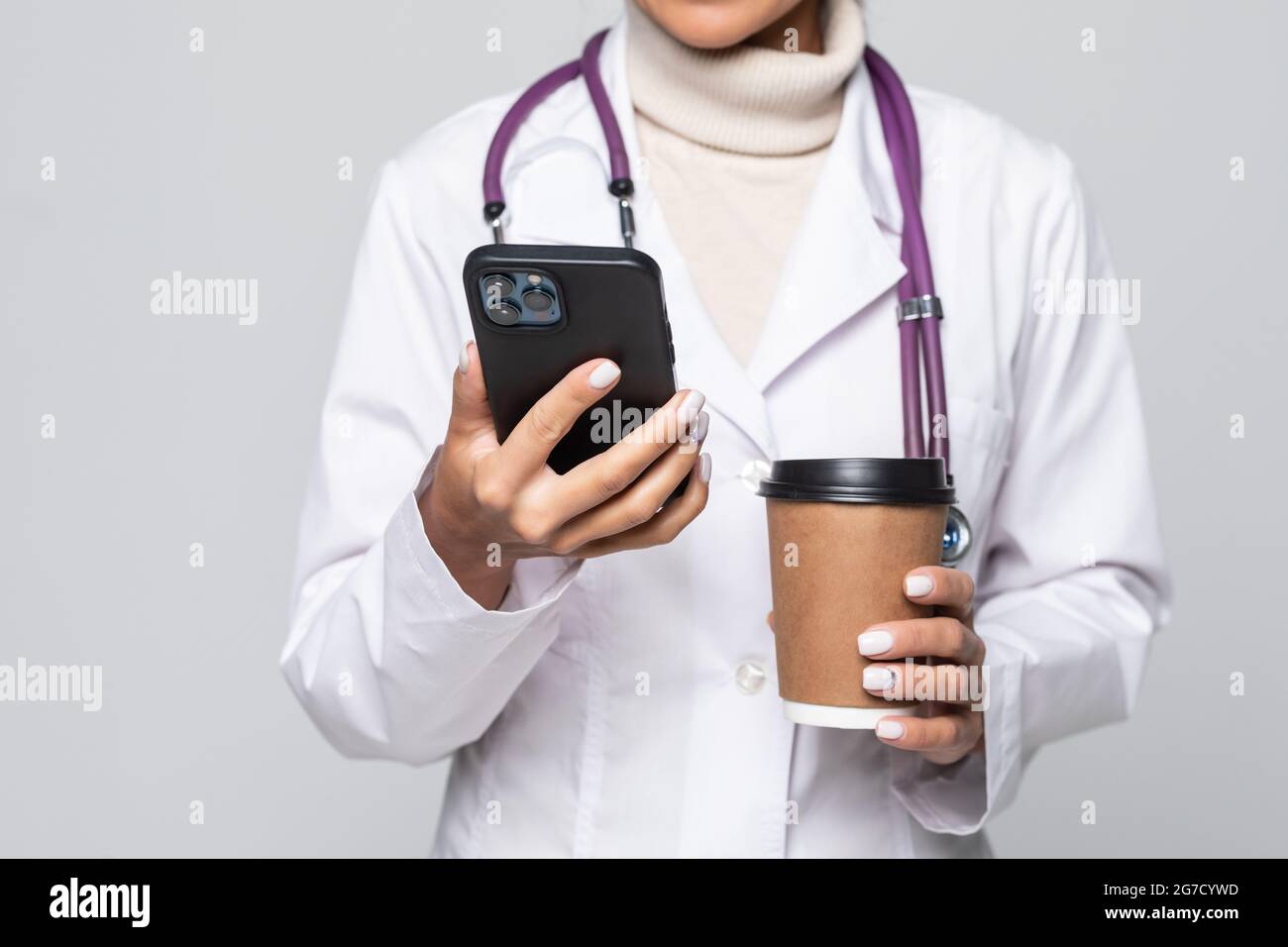Female doctor sitting with mobile phone and drinking coffee isolated on ...
