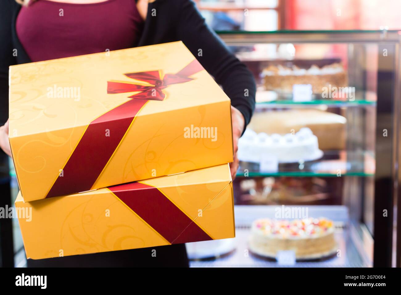 Woman presenting cake and pastries in takeaway boxes in cafe or pastry ...