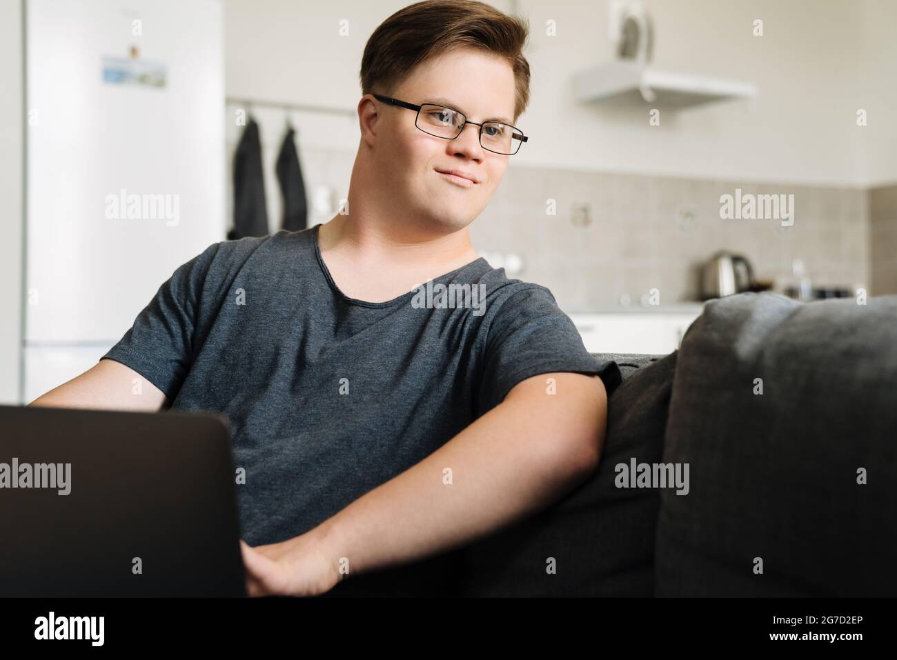 Young man with down syndrome using laptop while sitting on couch at ...