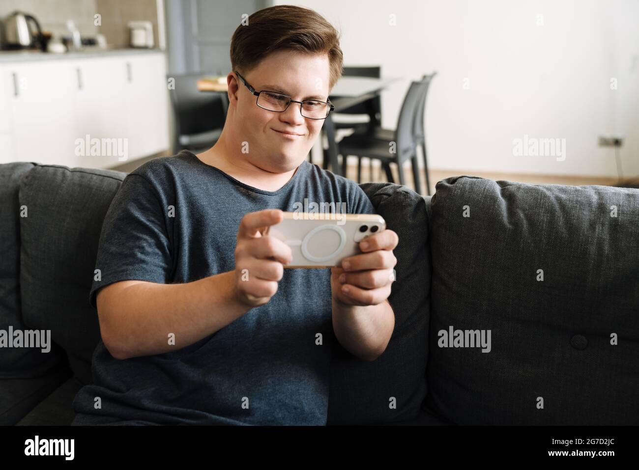 Young man with down syndrome using cellphone while sitting on couch at ...