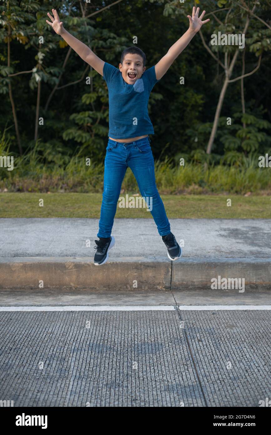 Vertical shot of an ecstatic Latino boy jumping joyfully with outspread ...