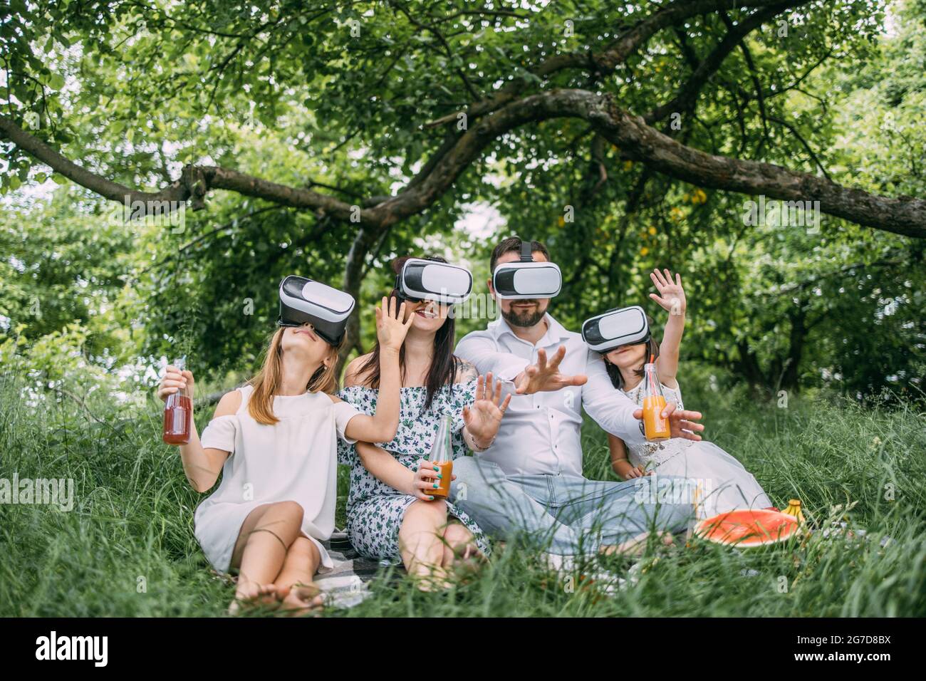 Parents and their two daughters wearing VR headset during picnic at ...