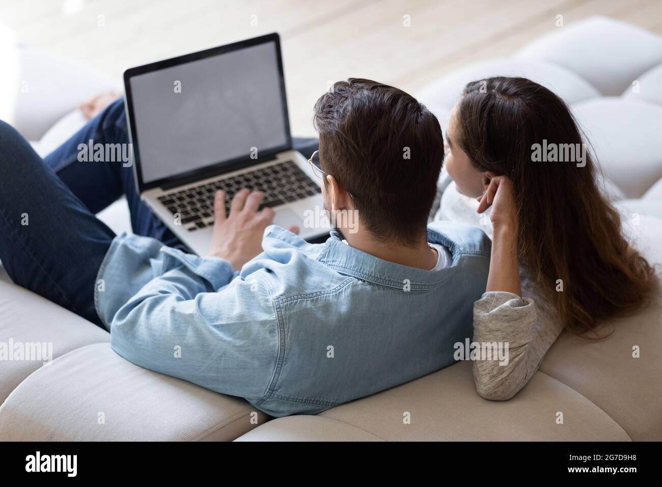 Rear view couple sit on sofa at home using computer Stock Photo - Alamy