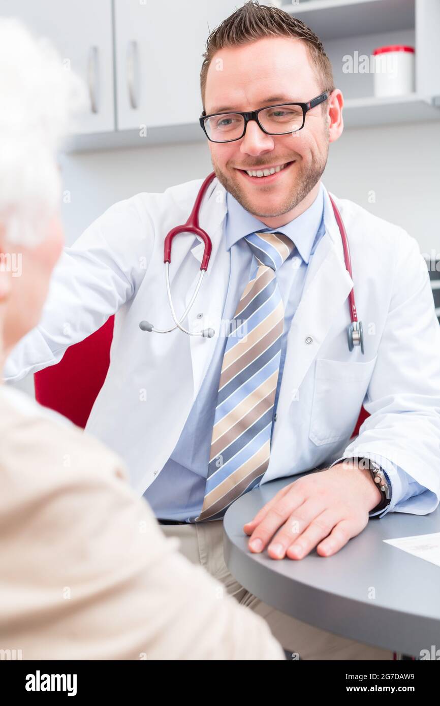 Doctor sitting with pensioner in surgery consultation hour at desk ...