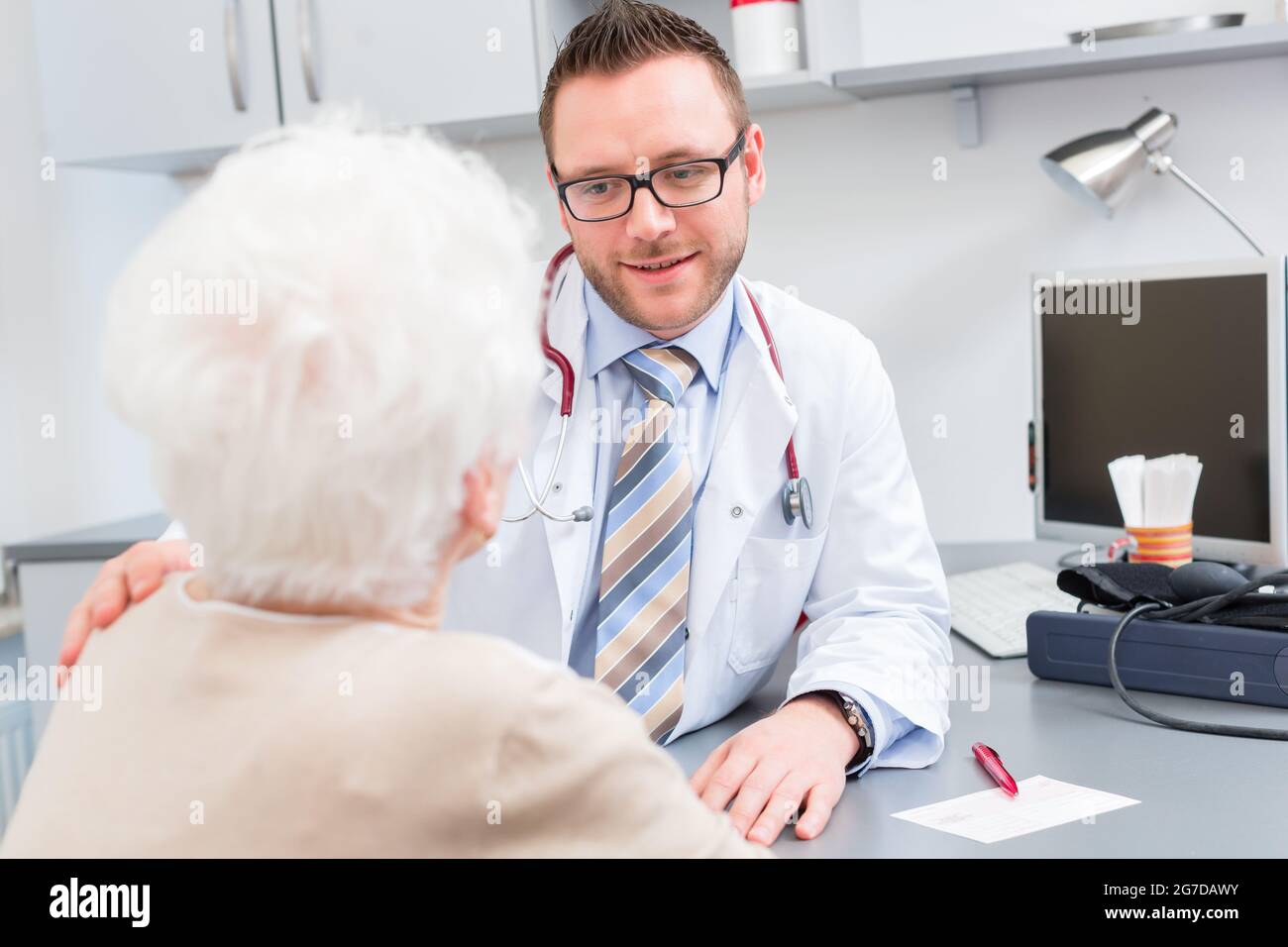 Doctor sitting with pensioner in surgery consultation hour at desk ...