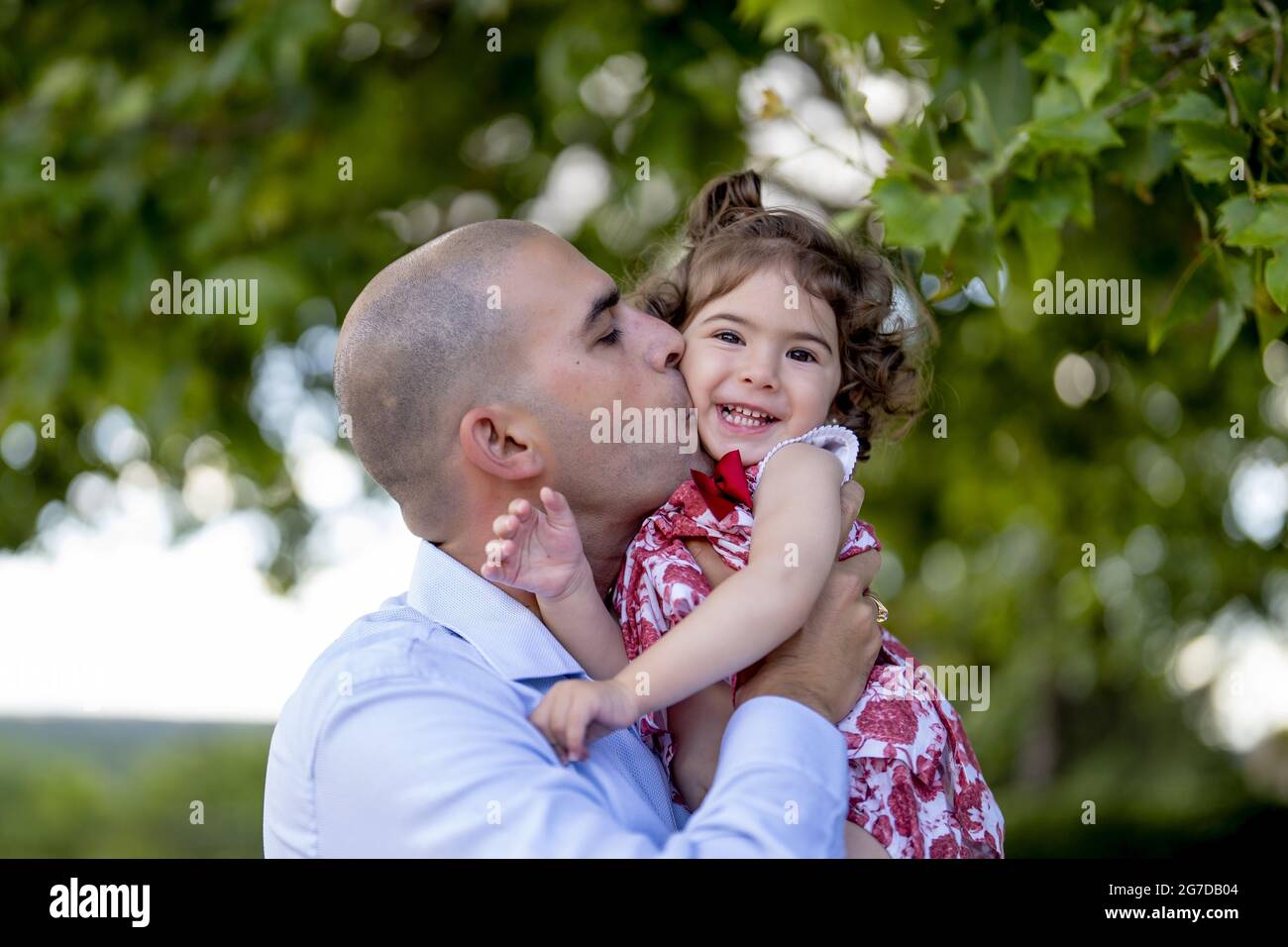 Father hugging and kissing her little daughter while walking in a park ...