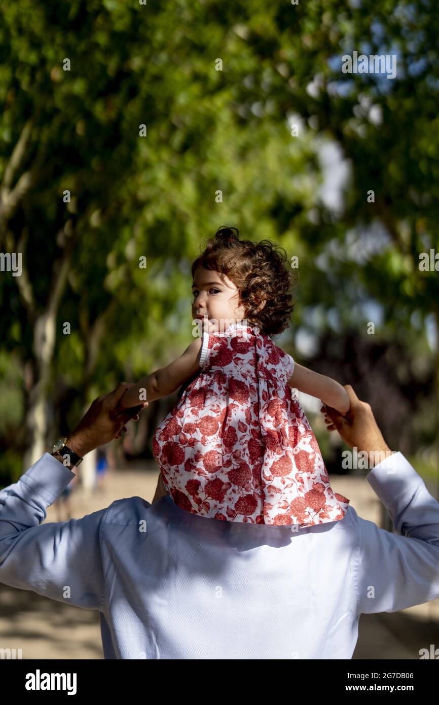 Vertical back view of the father carrying his daughter on his shoulders while in a park Stock ...