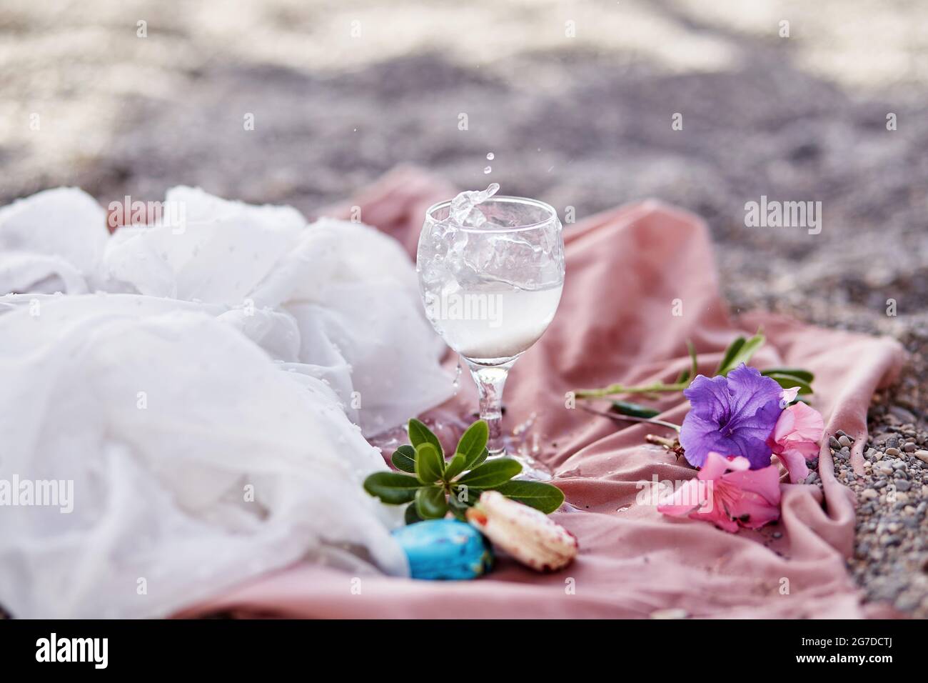 Gin tonic cocktail in wine glass on beach with flowers. Delicate silk materials and bokeh ...