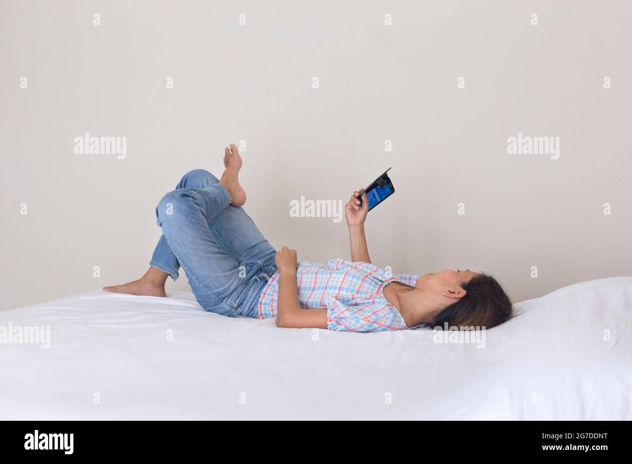 Female laying relaxing on bed holding up smart phone Stock Photo - Alamy