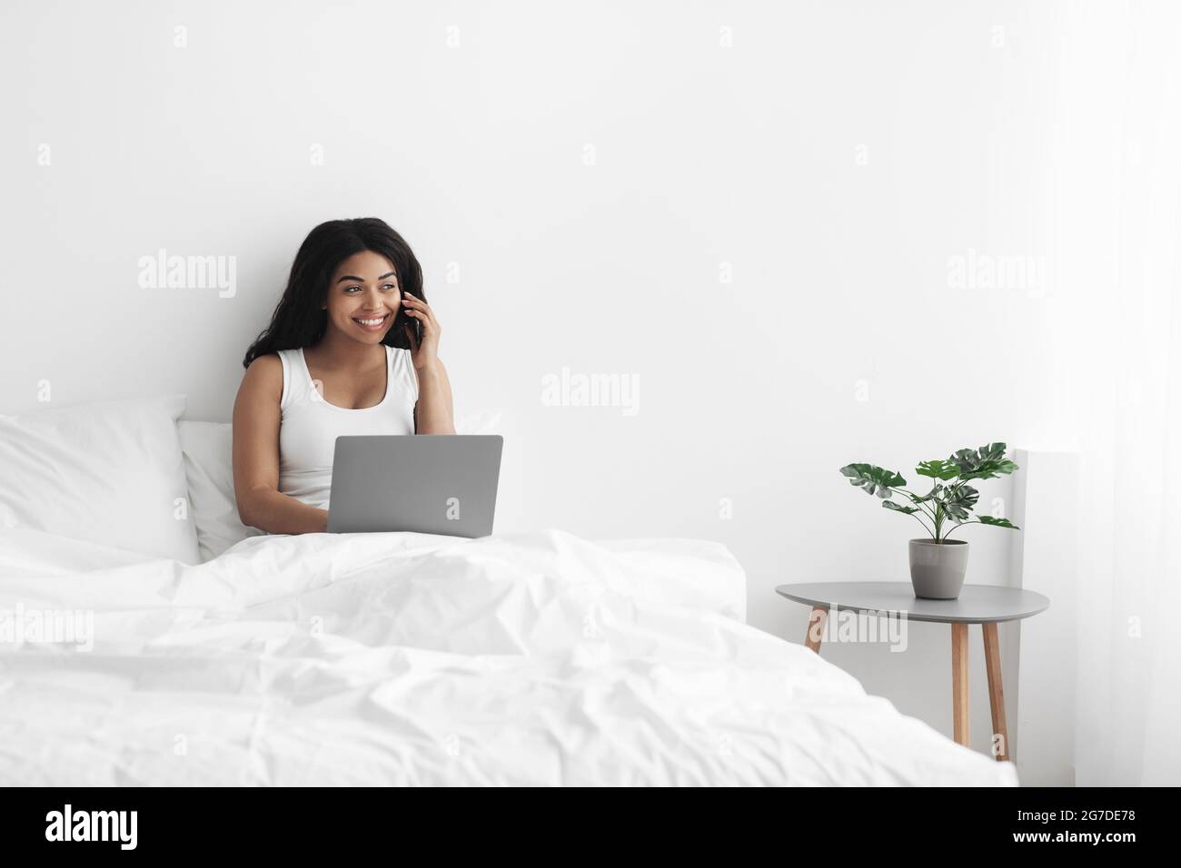 Multitasking. Happy black woman talking on smartphone and using laptop ...