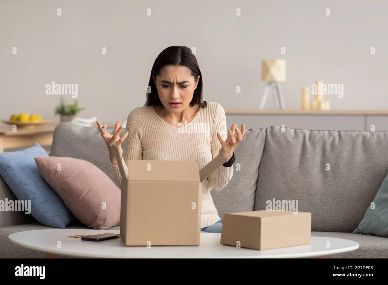 Angry confused woman unpacking parcel, wrong or broken online store ...