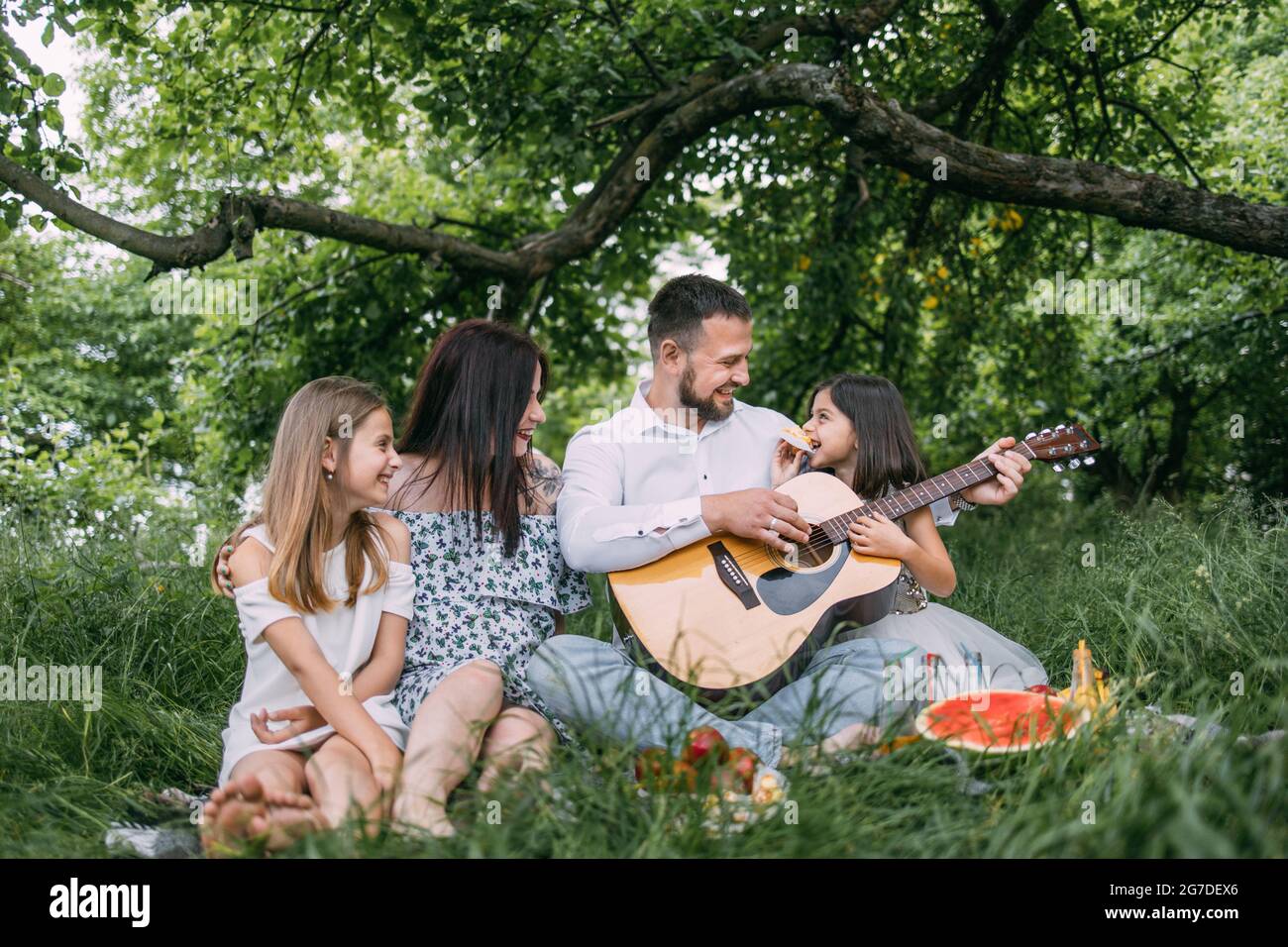 Happy parents with two child sitting on checkered blanket and singing ...