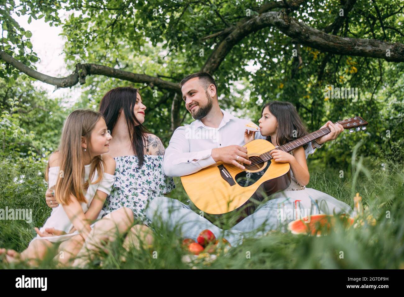 Happy parents with two child sitting on checkered blanket and singing ...