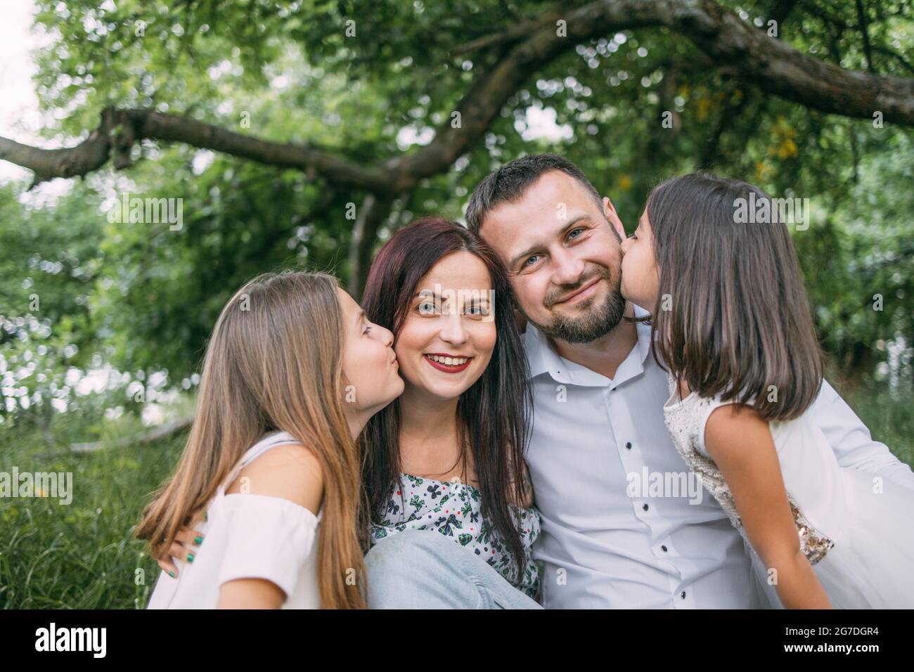 Two pretty sisters kissing their father and mother during summer picnic ...
