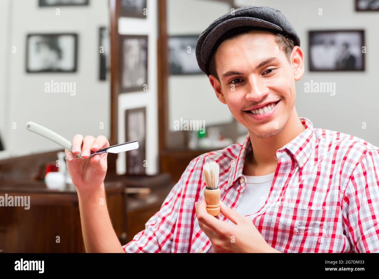 Portrait of smiling hairdresser holding razor and shaving brush in ...