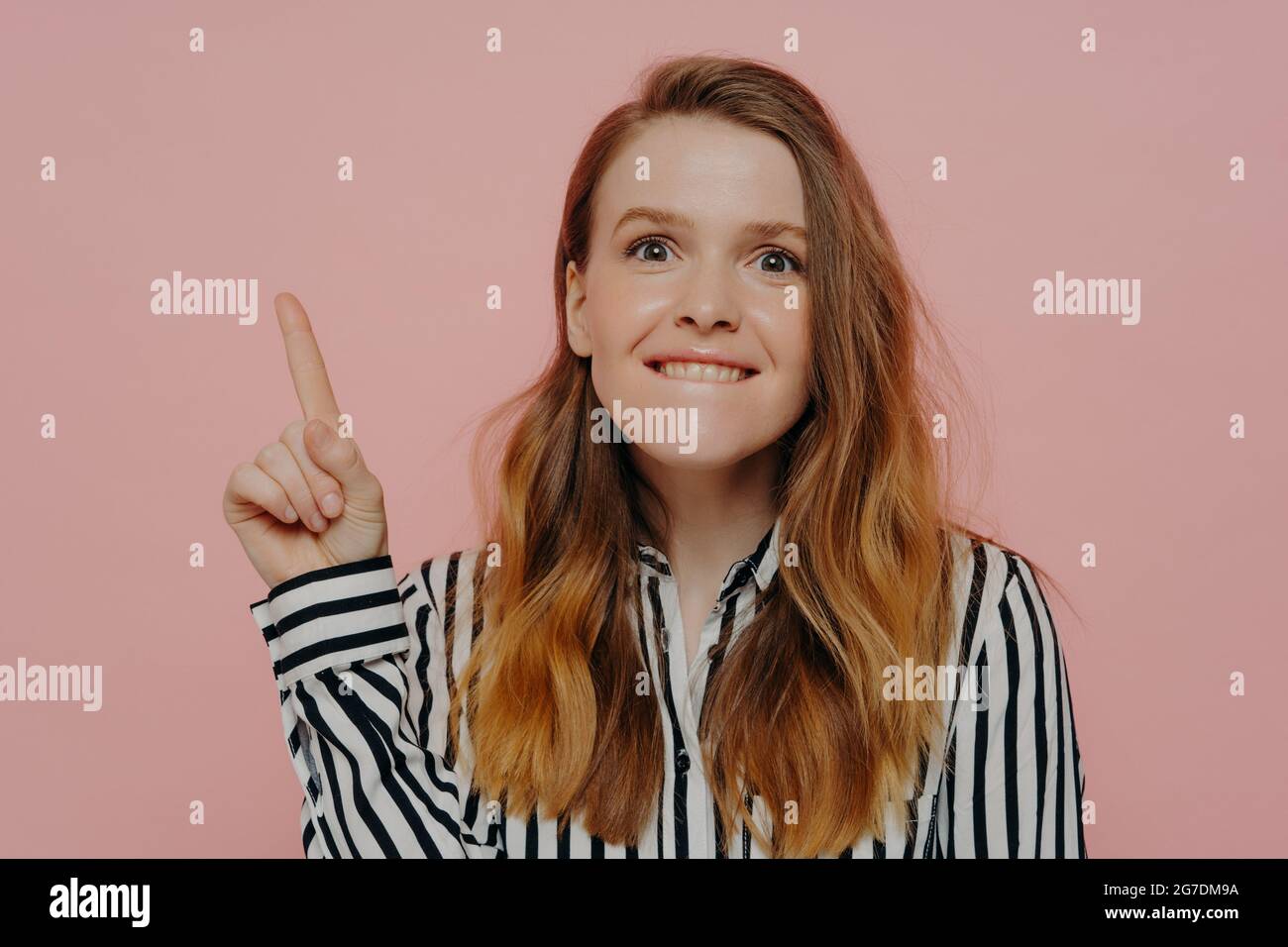 Young excited woman biting lip and pointing up at copy space Stock ...