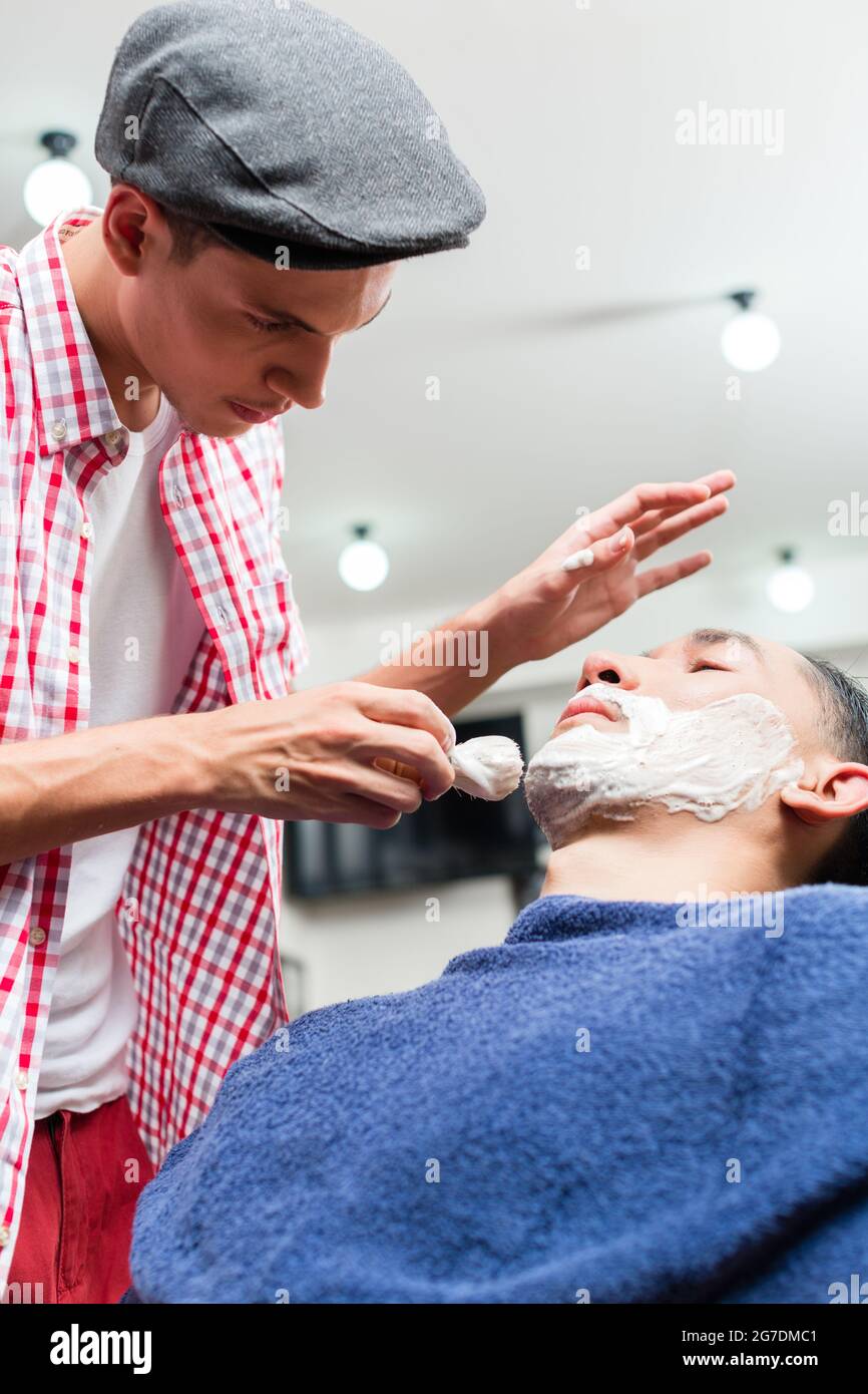 Barber putting some shaving cream on a client before shaving his beard ...