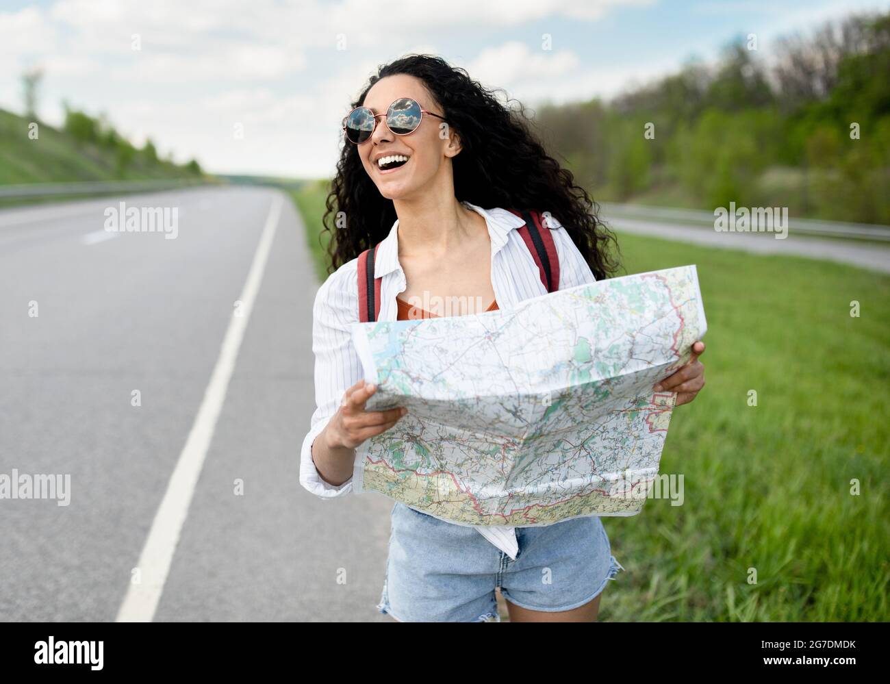 Joyful millennial lady walking along asphalt road with map, choosing ...