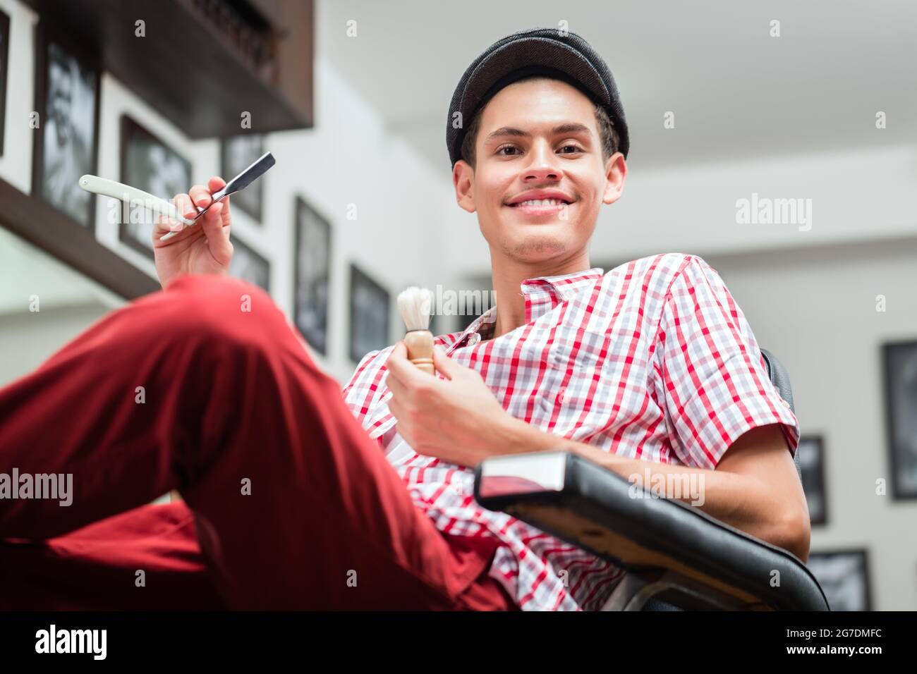 Portrait of smiling hairdresser holding razor and shaving brush sitting ...