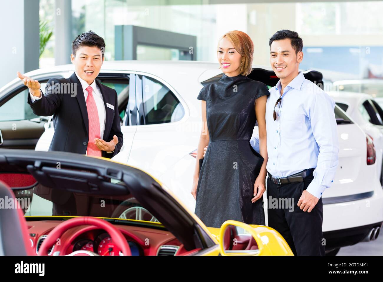 Asian couple buying car in auto dealership consulting the salesman ...