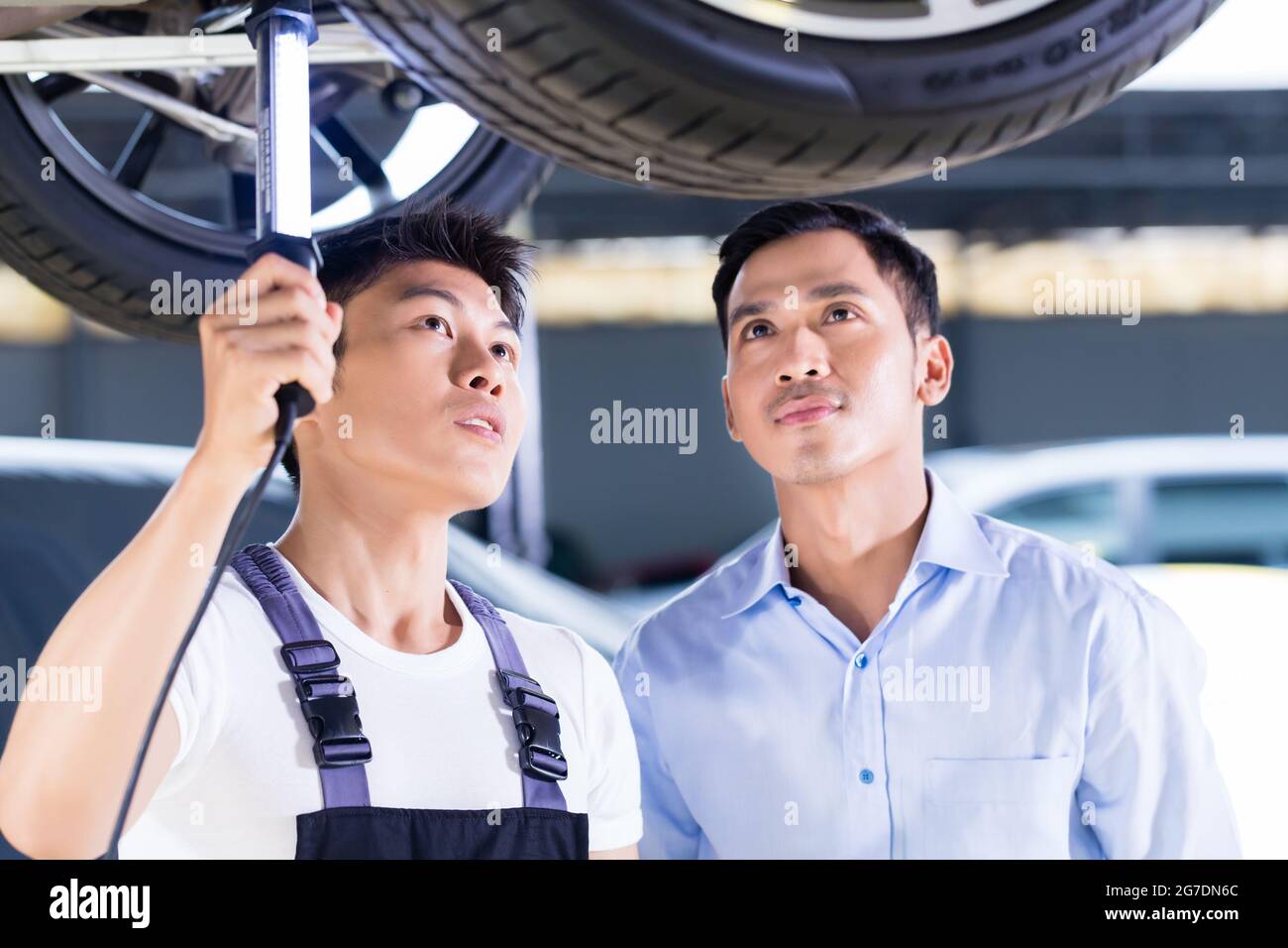 Asian Chinese car mechanic with customer looking at auto floor with ...